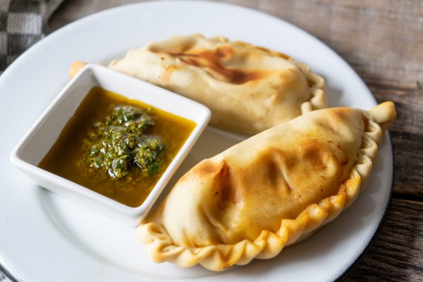 Argentine empanadas with chimichurri sauce on wooden background - The ...